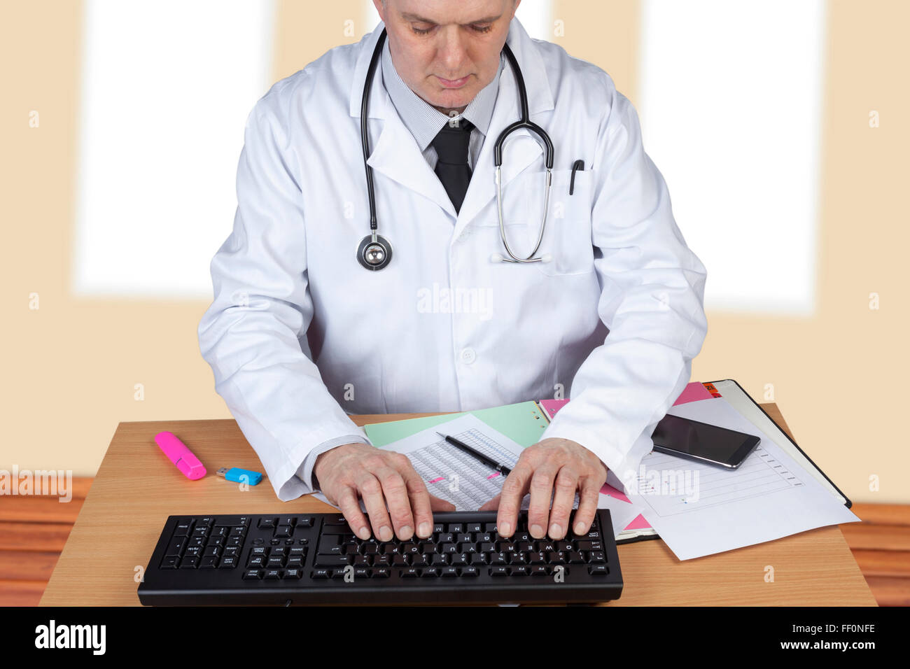 Doctor with stethoscope around his neck typing up a report on his ...