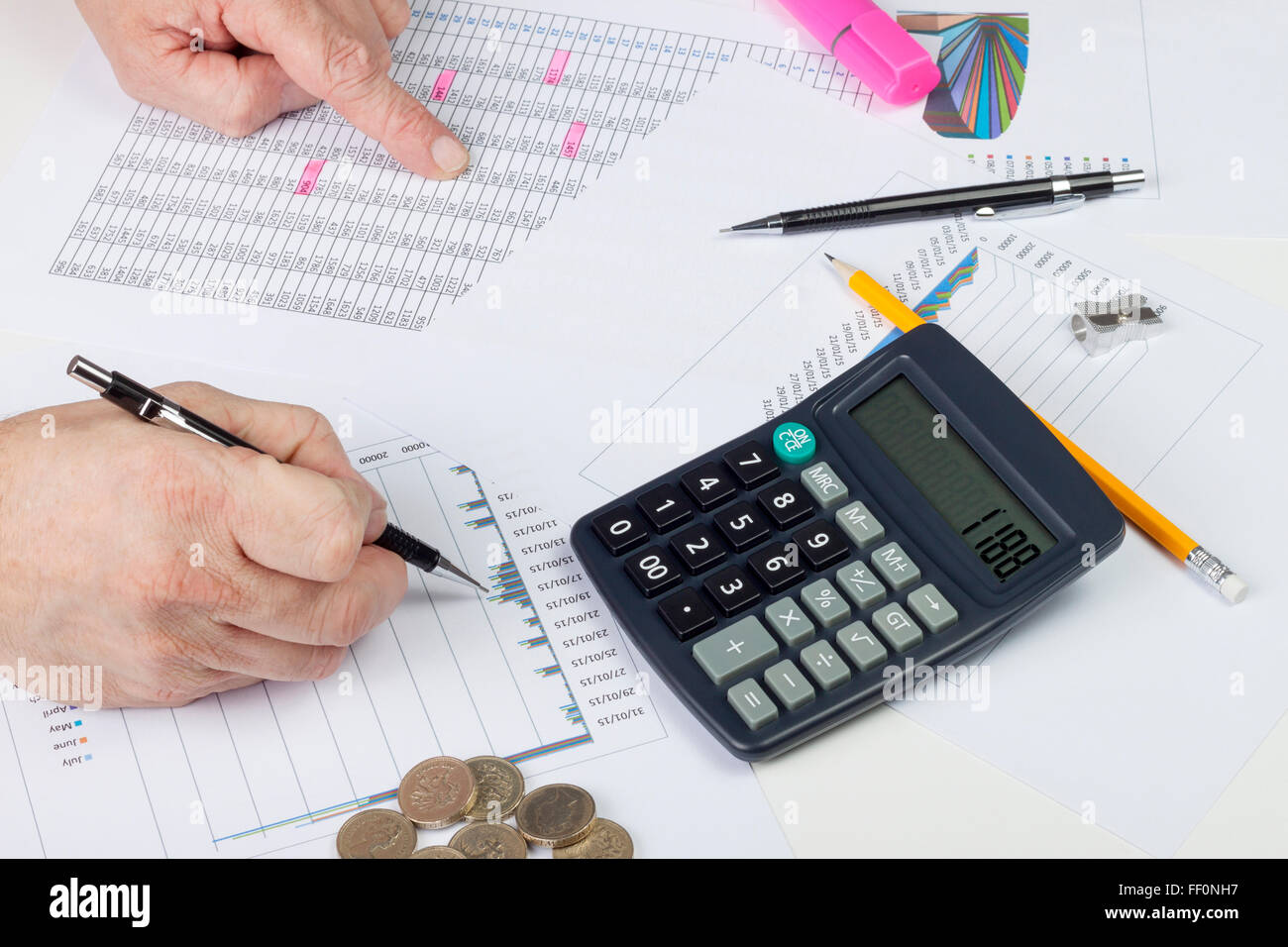 Account at his desk cross checking data with graphs and a calculator ...