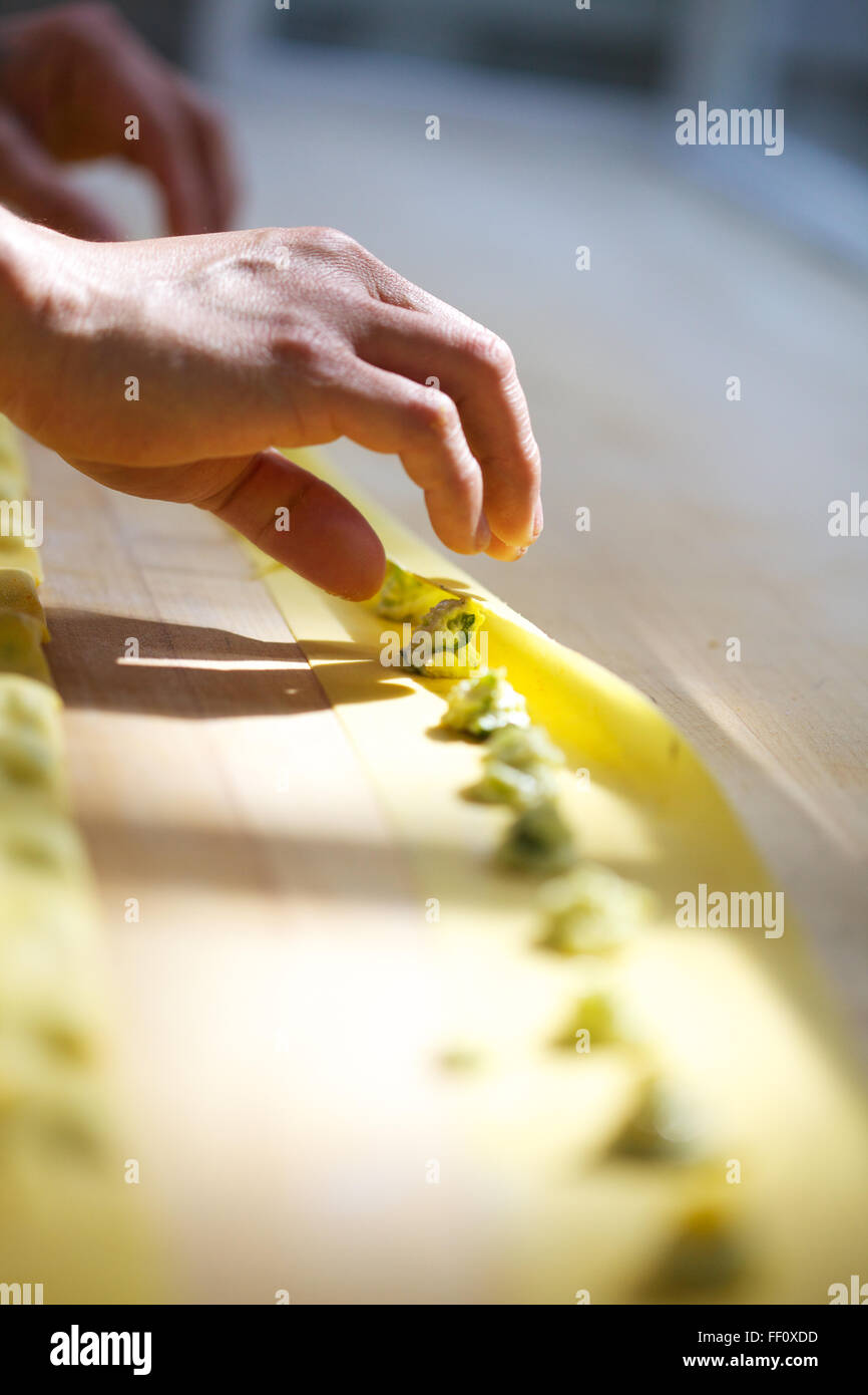 A close-up on hands folding homemade pasta dough over small dots of ...