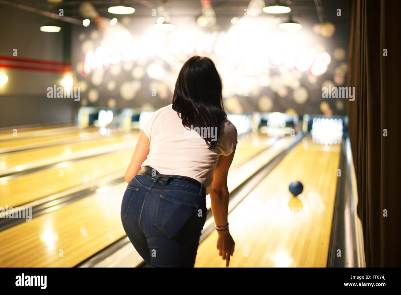 The back of a woman bowling in a brightly lit bowling alley, ball is ...