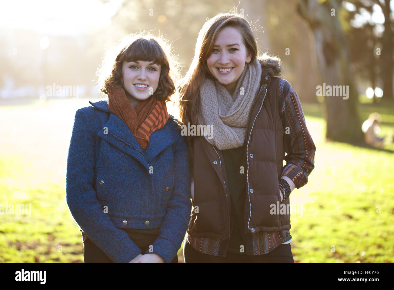Two young lady friends standing side by side, smiling at the camera ...