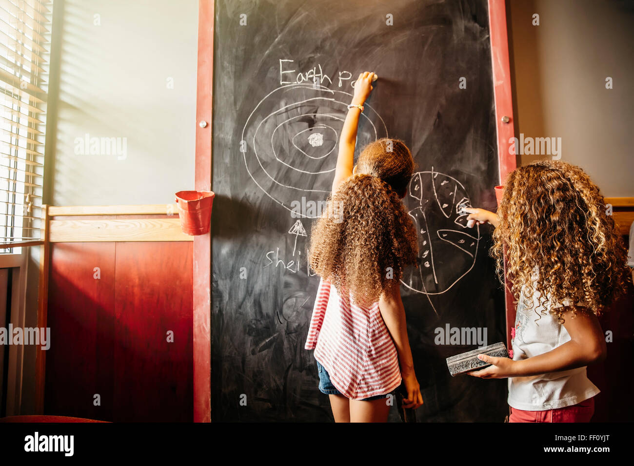 Mixed race sisters drawing on chalkboard Stock Photo - Alamy