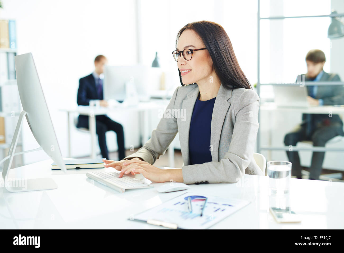 Pretty secretary in front of computer typing in working environment ...