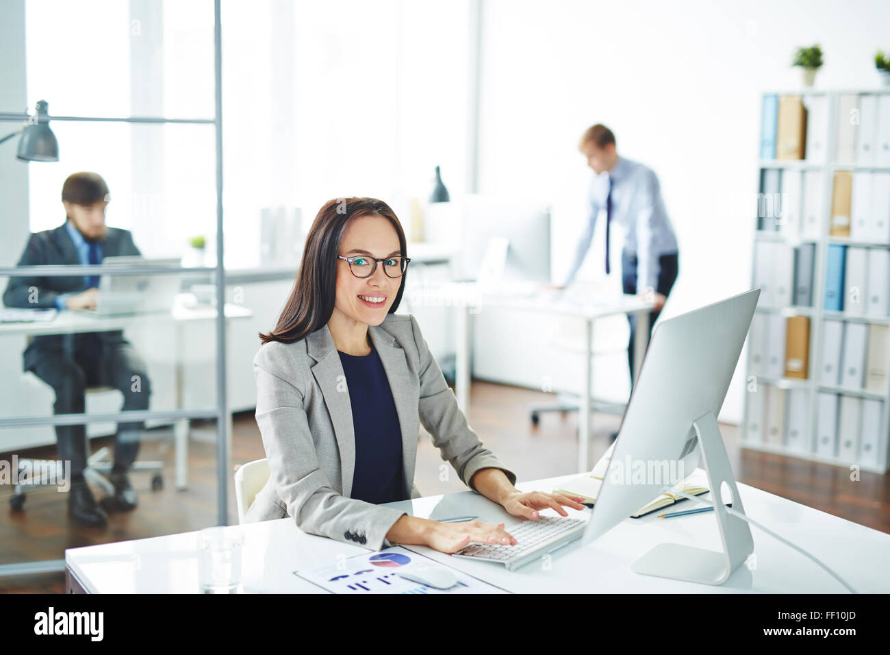 Pretty secretary looking at camera at workplace in front of computer ...