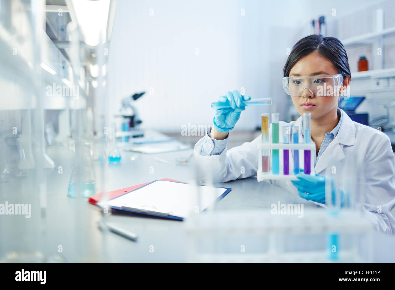 Female assistant analyzing fluids in flasks in scientific laboratory ...