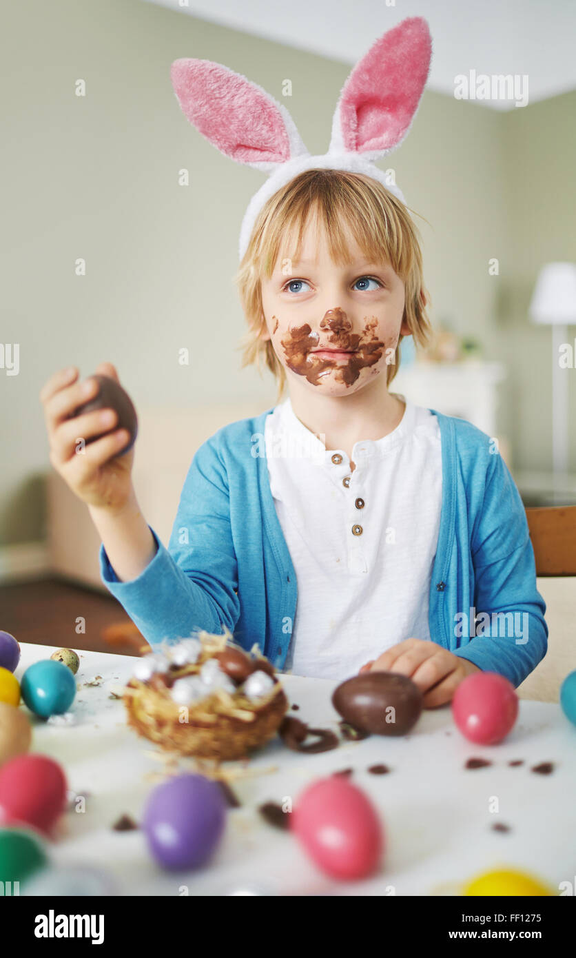 Cute boy with rabbit ears eating chocolate Easter eggs Stock Photo - Alamy
