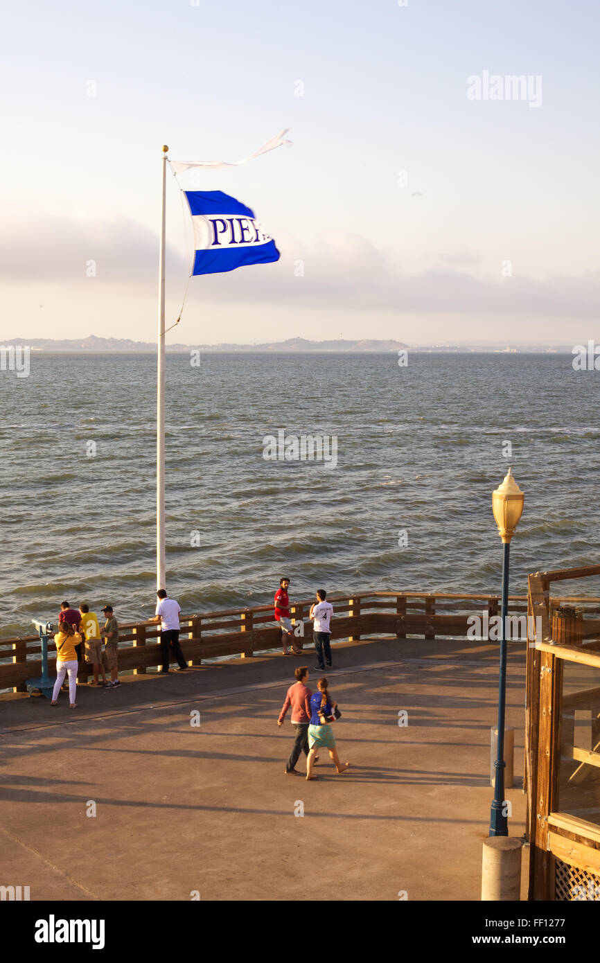 A couple int the foreground walk along a waterfront pier while people ...