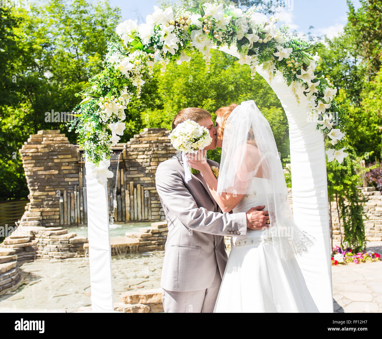 First kiss of newly married couple under wedding arch Stock Photo - Alamy
