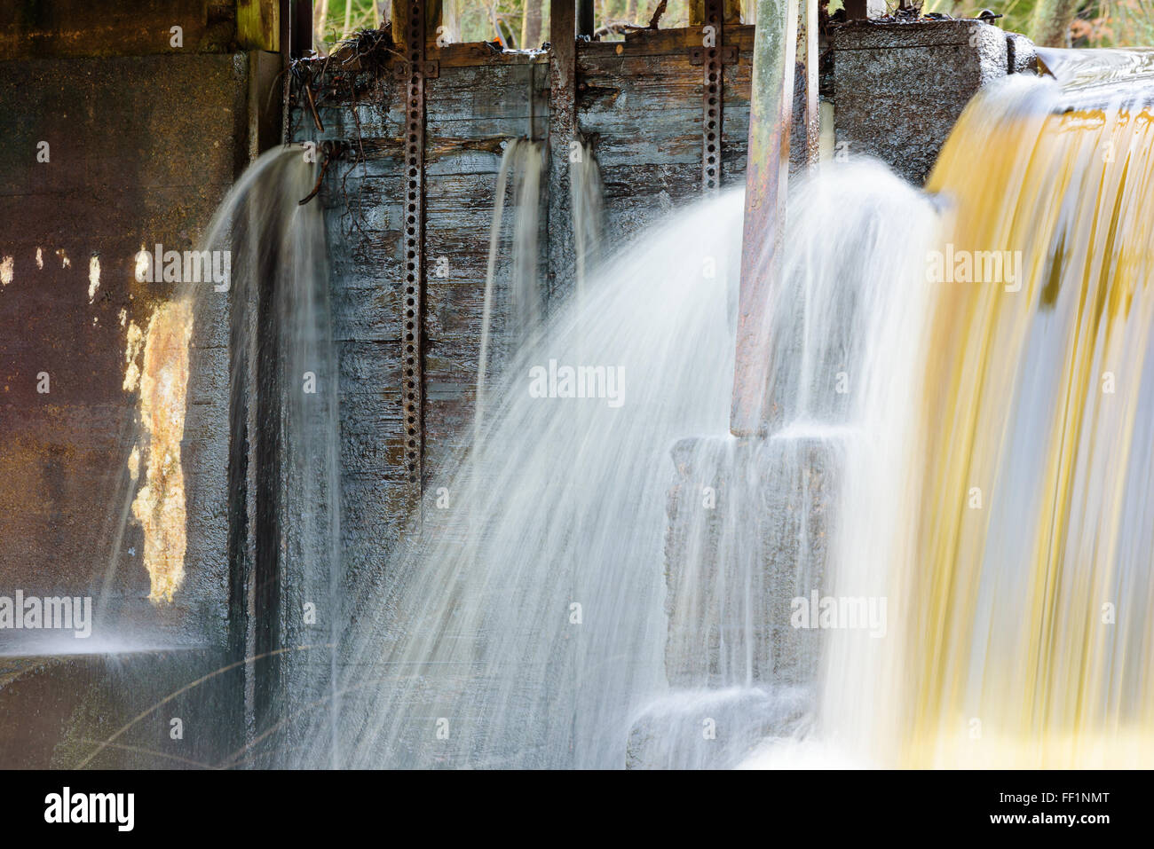 Water cascading out over the edge of a small dam. Water is brownish and ...