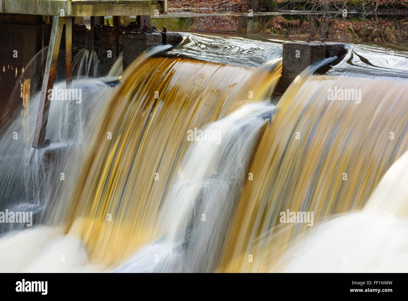 Water cascading out over the edge of a small dam. Water is brownish and ...