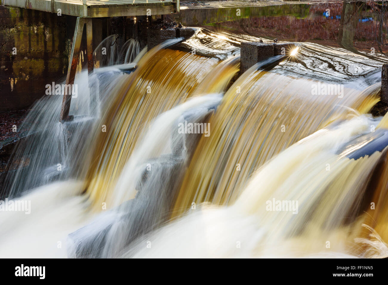 Water cascading out over the edge of a small dam. Water is brownish and ...