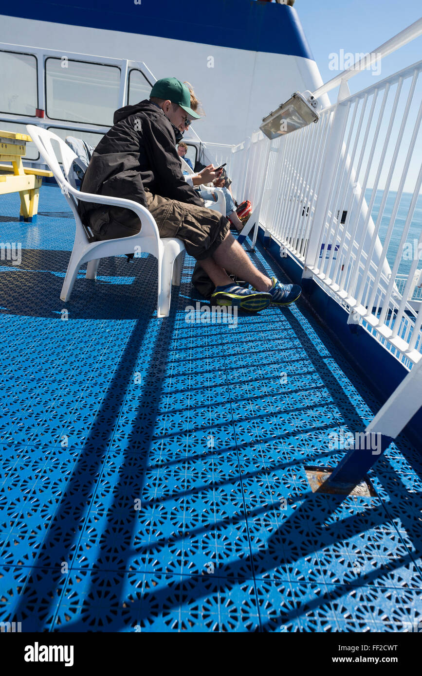 Ferry passengers on upper deck in the sun sitting on chairs looking on ...