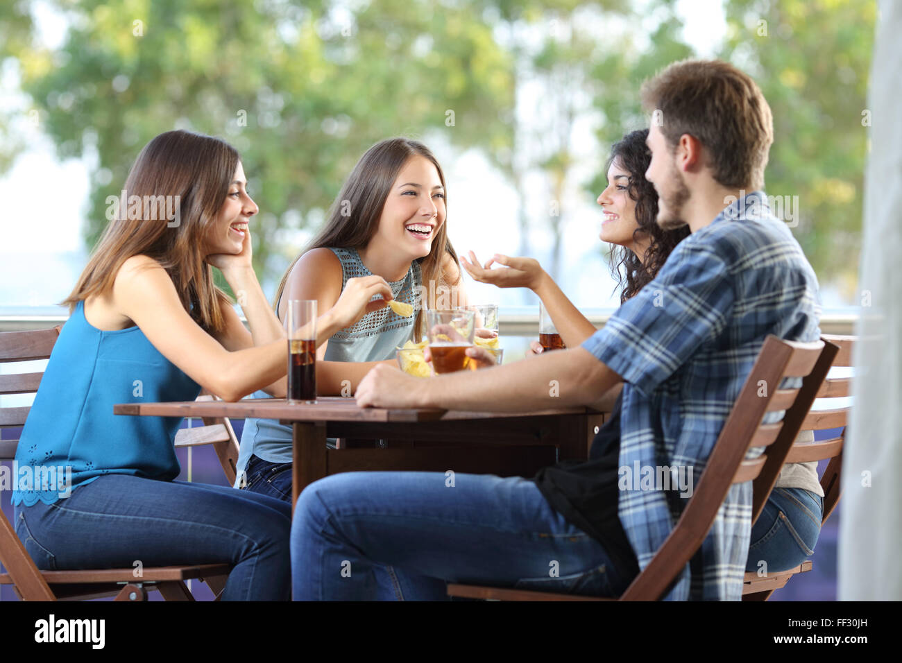 Group of four friends talking and drinking sitting in a terrace at home ...