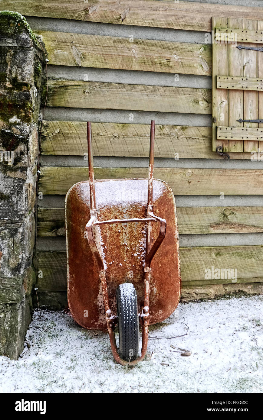 An old red wheelbarrow against the side of a log cabin in the winter ...