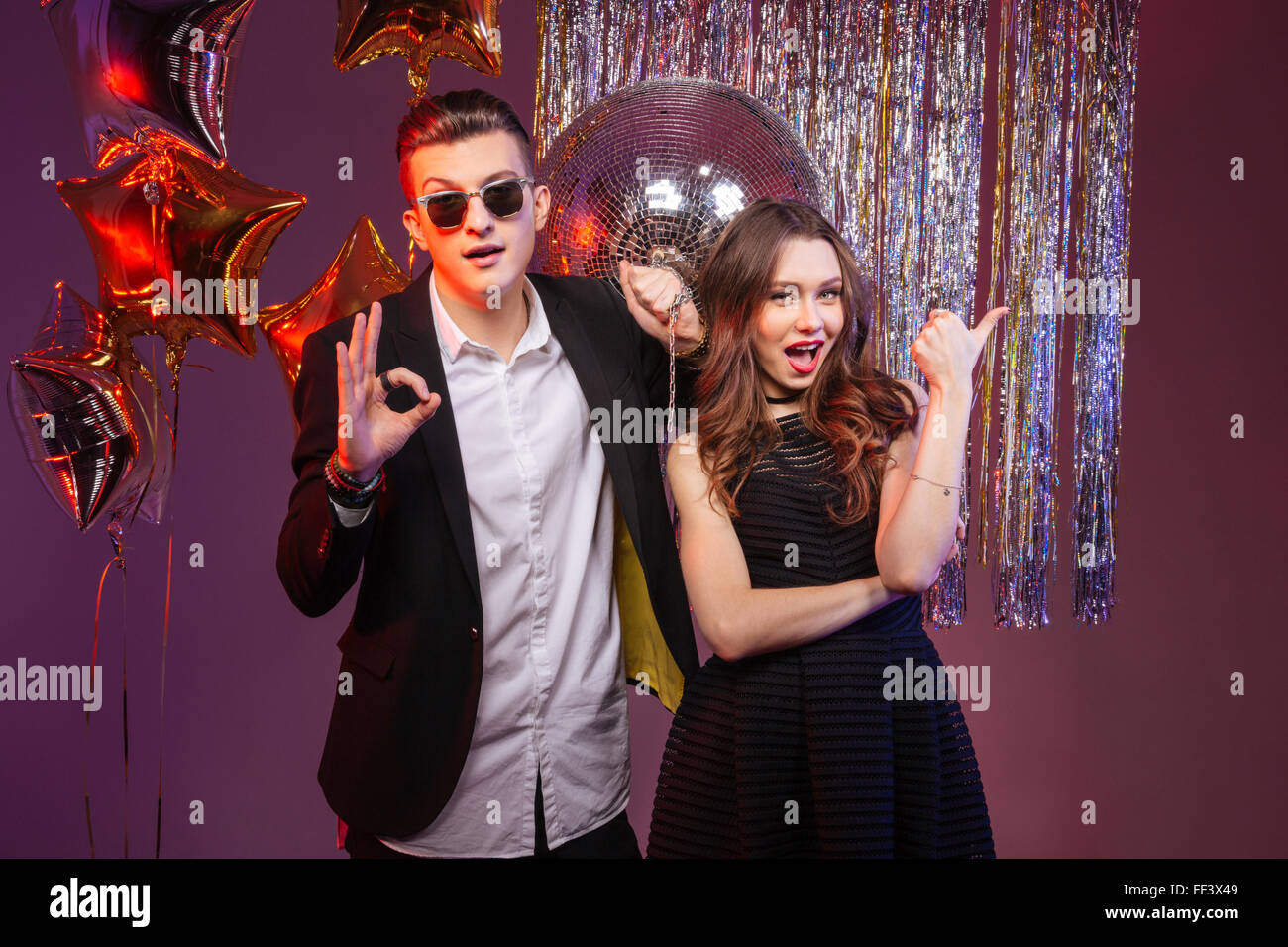 Beautiful young couple having party and showing thumbs up and ok ...