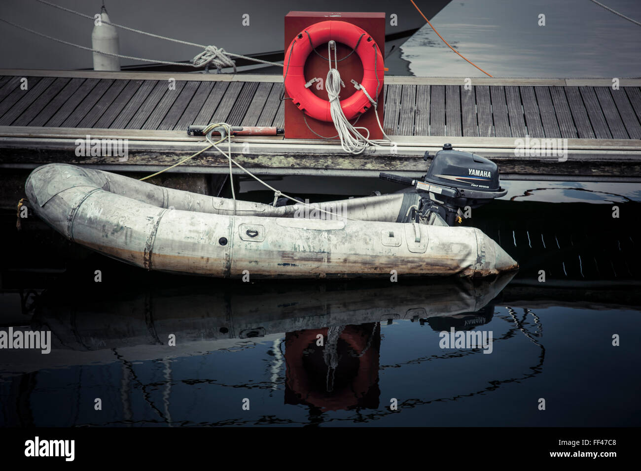 A dirty, stained inflatable rubber dinghy tied up at a wooden jetty in ...