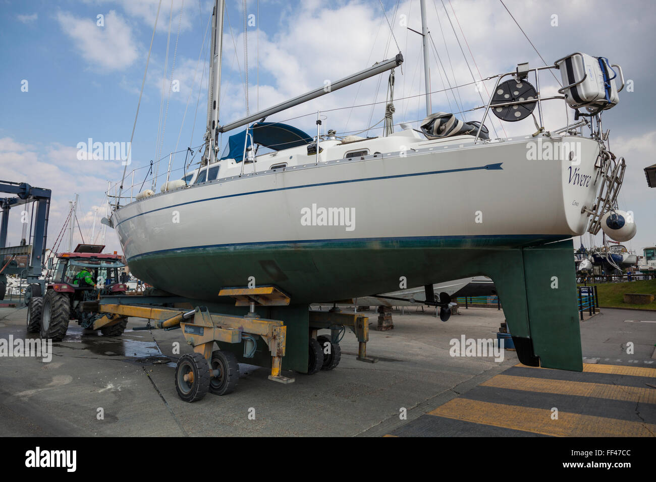 A tractor tows a large yacht on a trailer towards the water in a marina ...