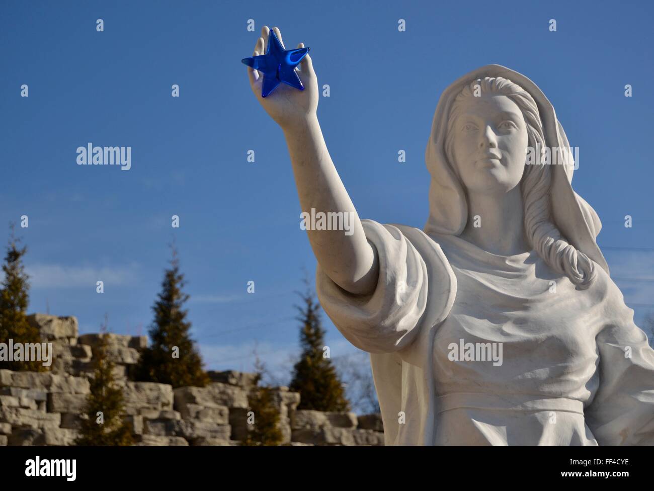 This is a statue of a lady holding up a blue star in her hand against a ...