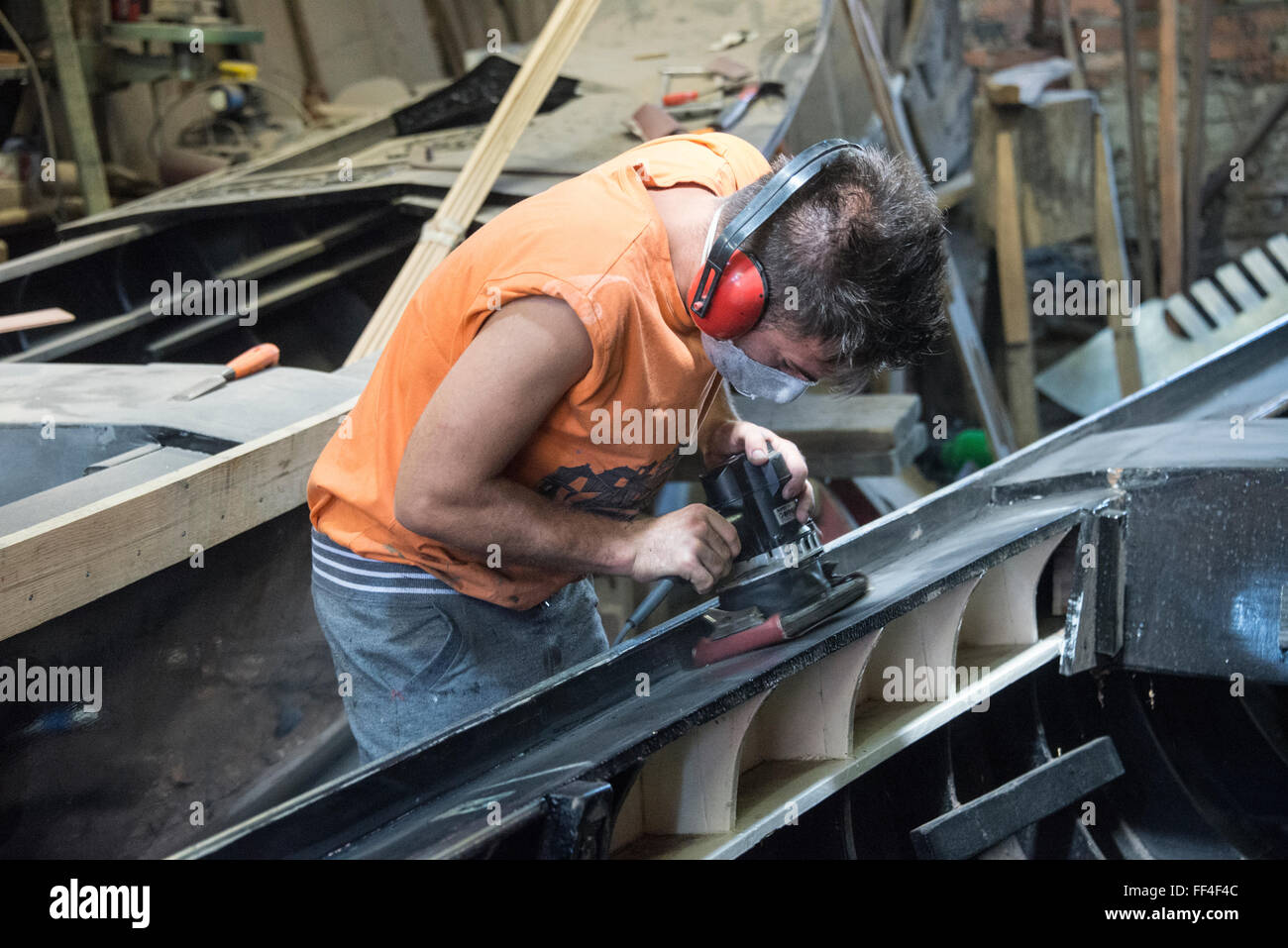 A gondola craftsman wearing protective face masks, sanding a black ...