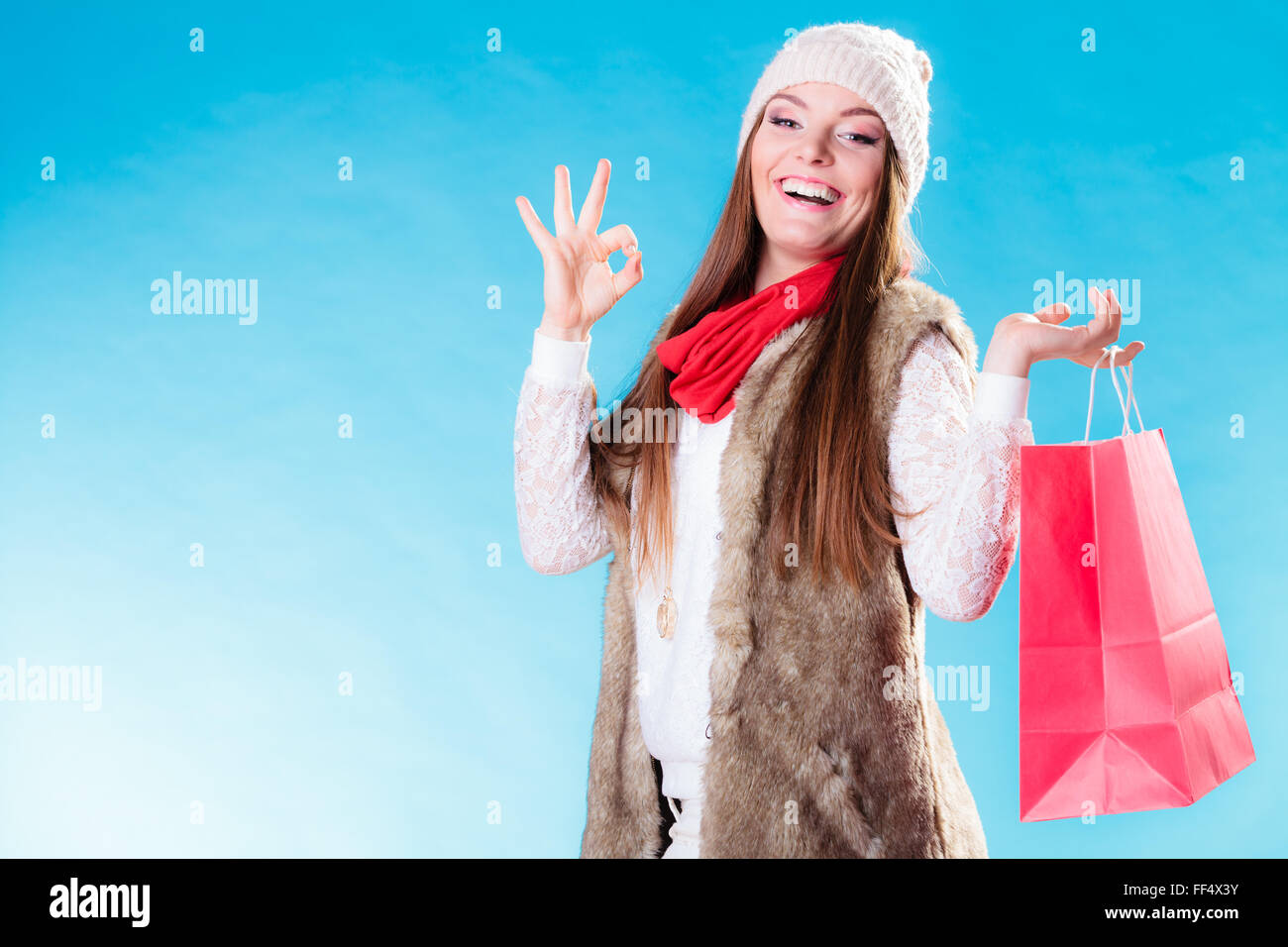 Winter woman in warm clothing with red paper shopping bag showing ok ...