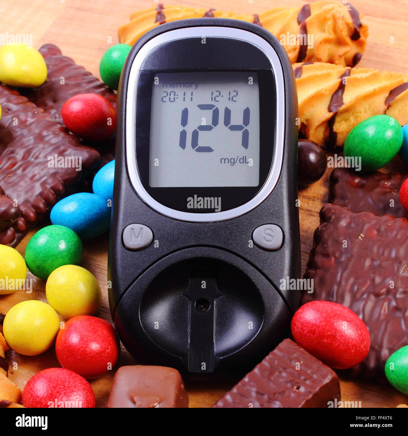 Glucose meter with heap of candies and cookies on wooden table, too ...