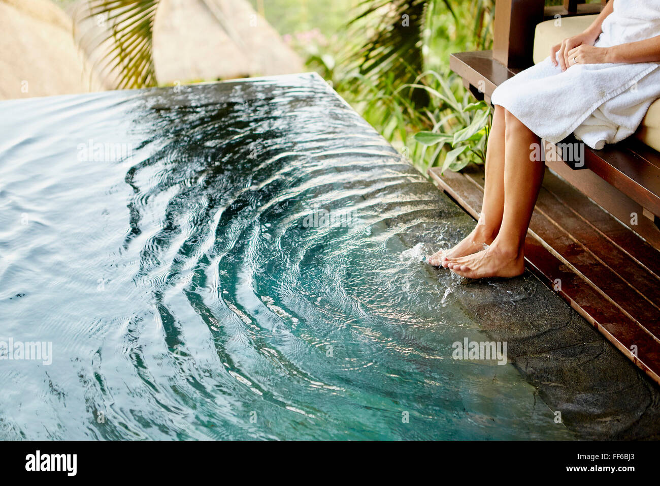 A person sitting on a bench with her feet in the shallow water of a ...