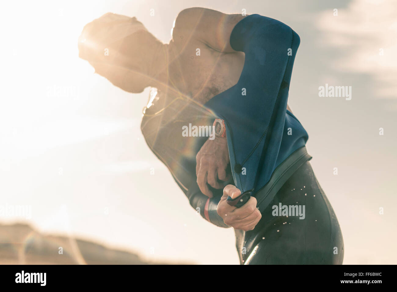 A swimmer in a wet suit on the beach, taking off one layer of clothing ...