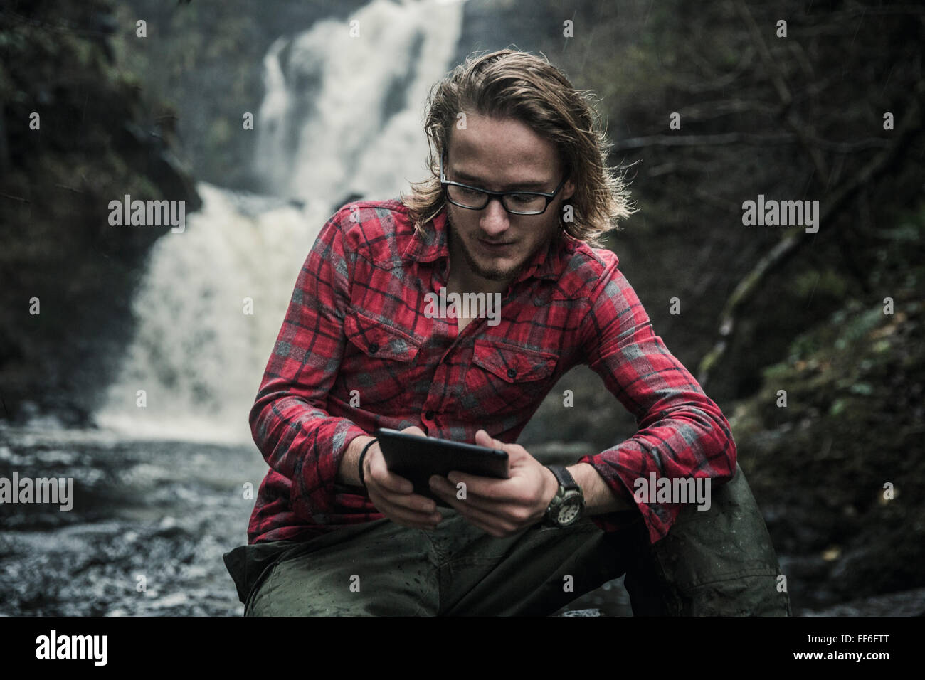 A man sitting by a fast flowing stream using a digital tablet Stock ...