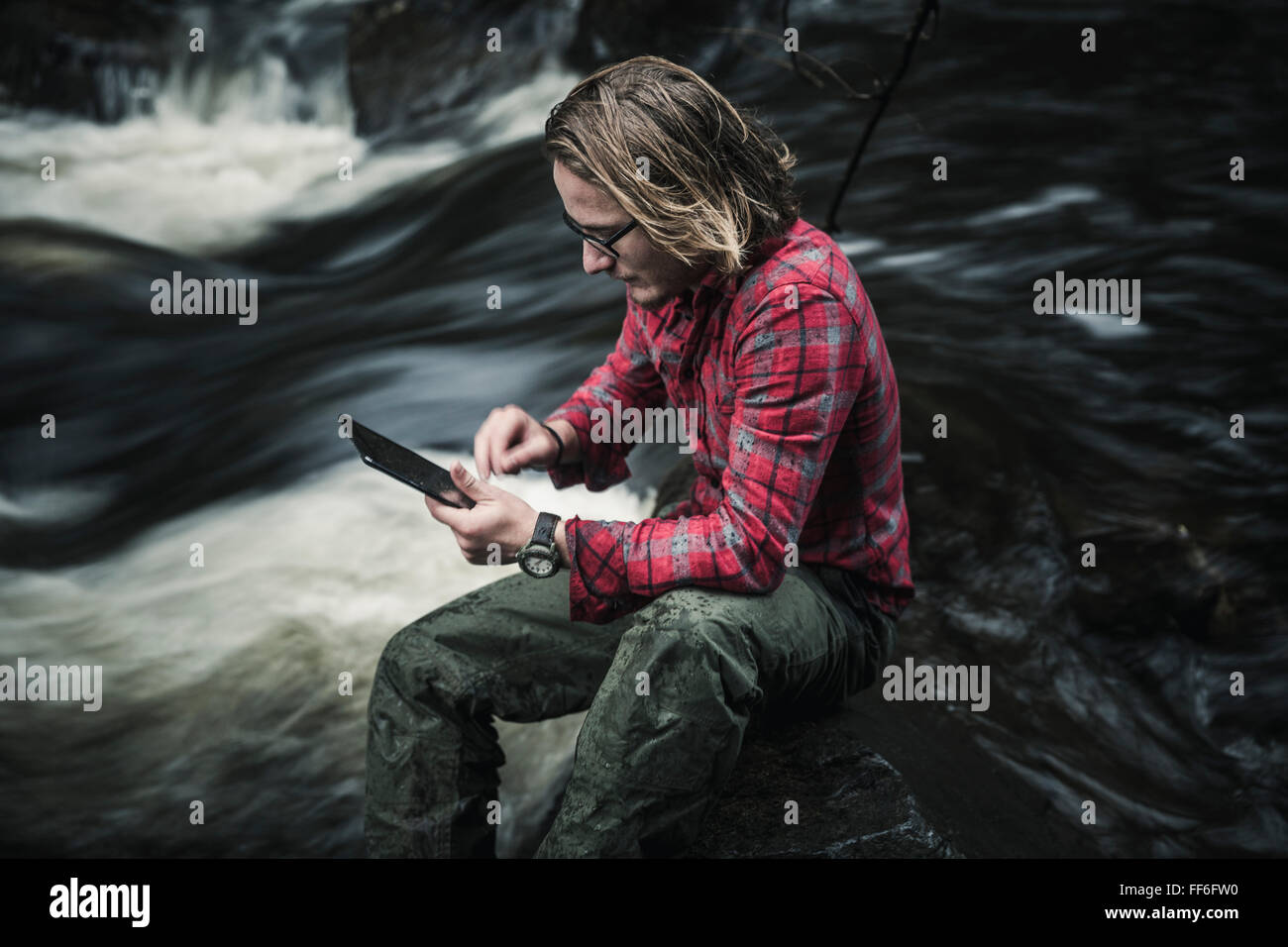 A man sitting by a fast flowing stream using a digital tablet Stock ...
