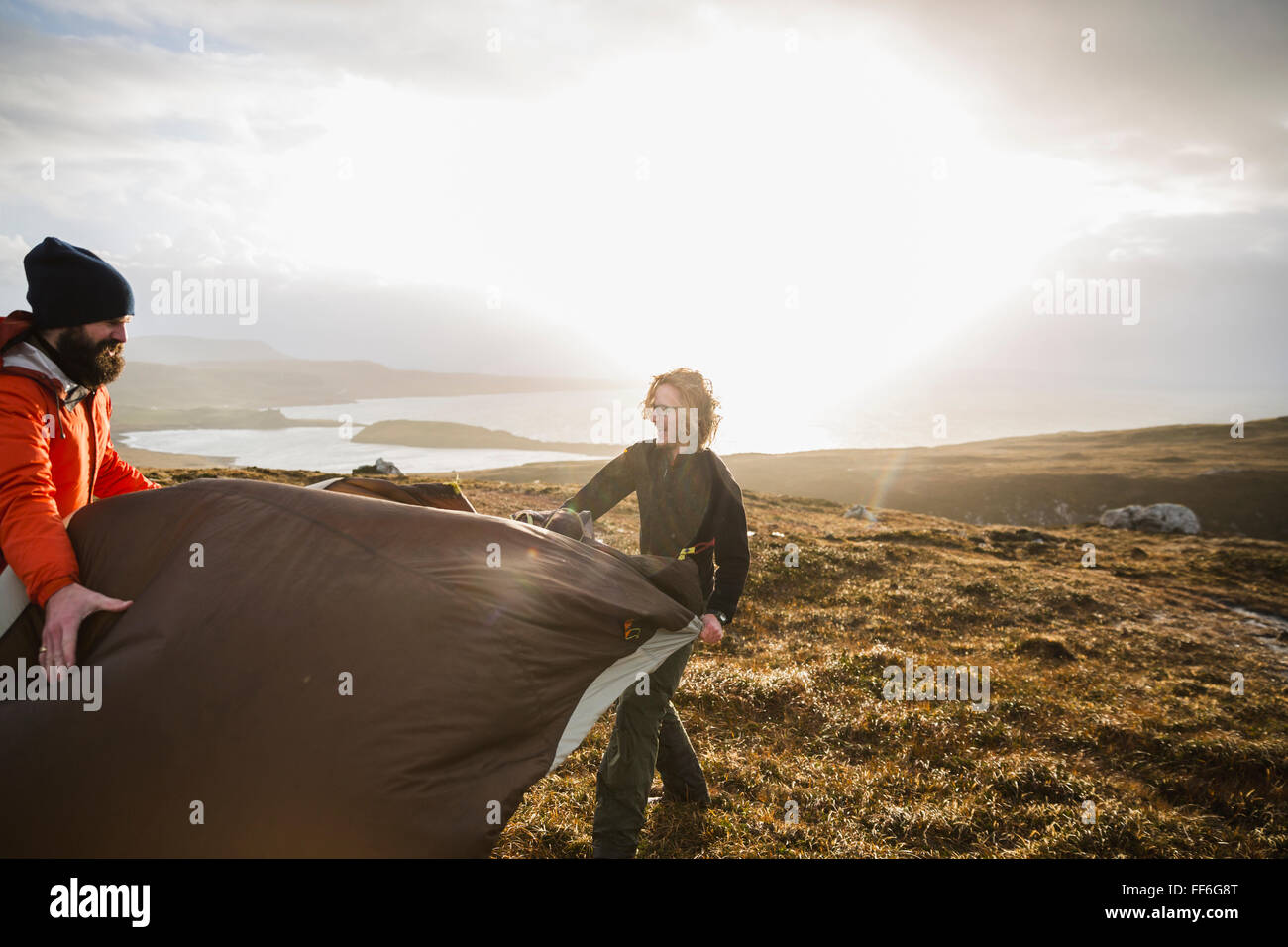 Two men holding and putting up a small tent in open space. Wild camping ...