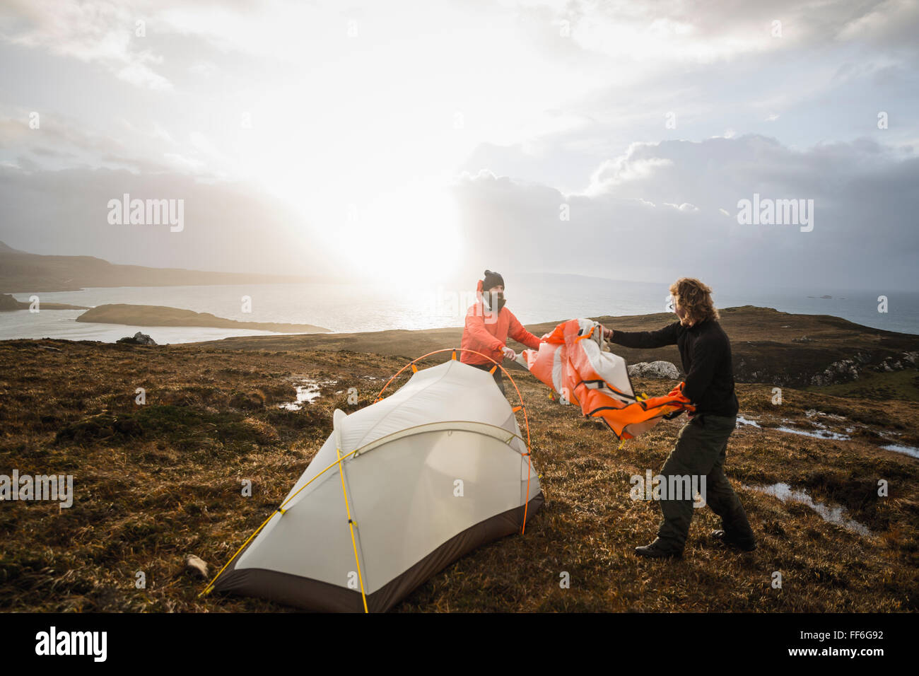 Two men holding and putting up a small tent in open space. Wild camping ...