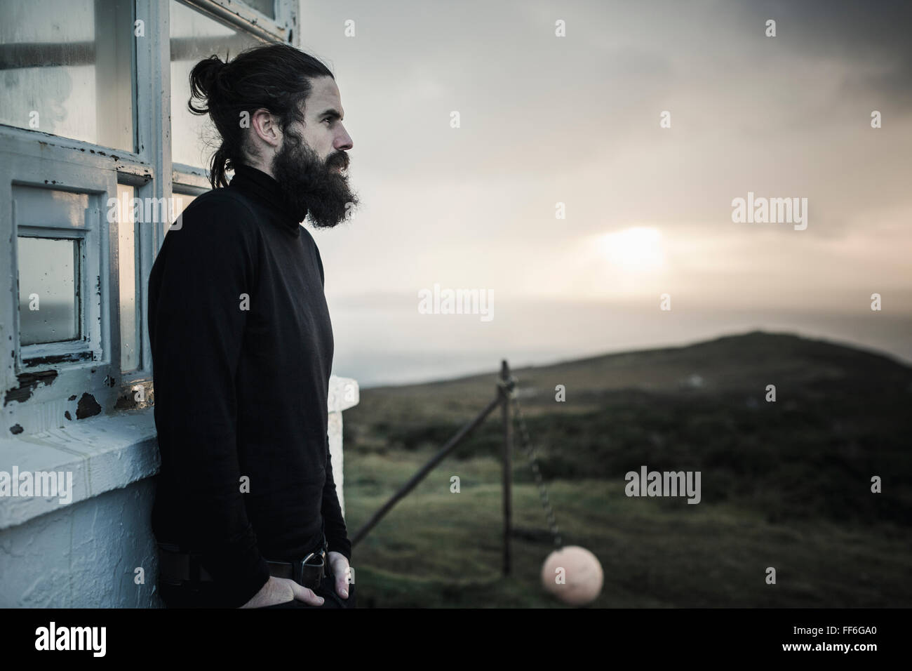 A man standing outside a building, looking at the darkening sky at ...