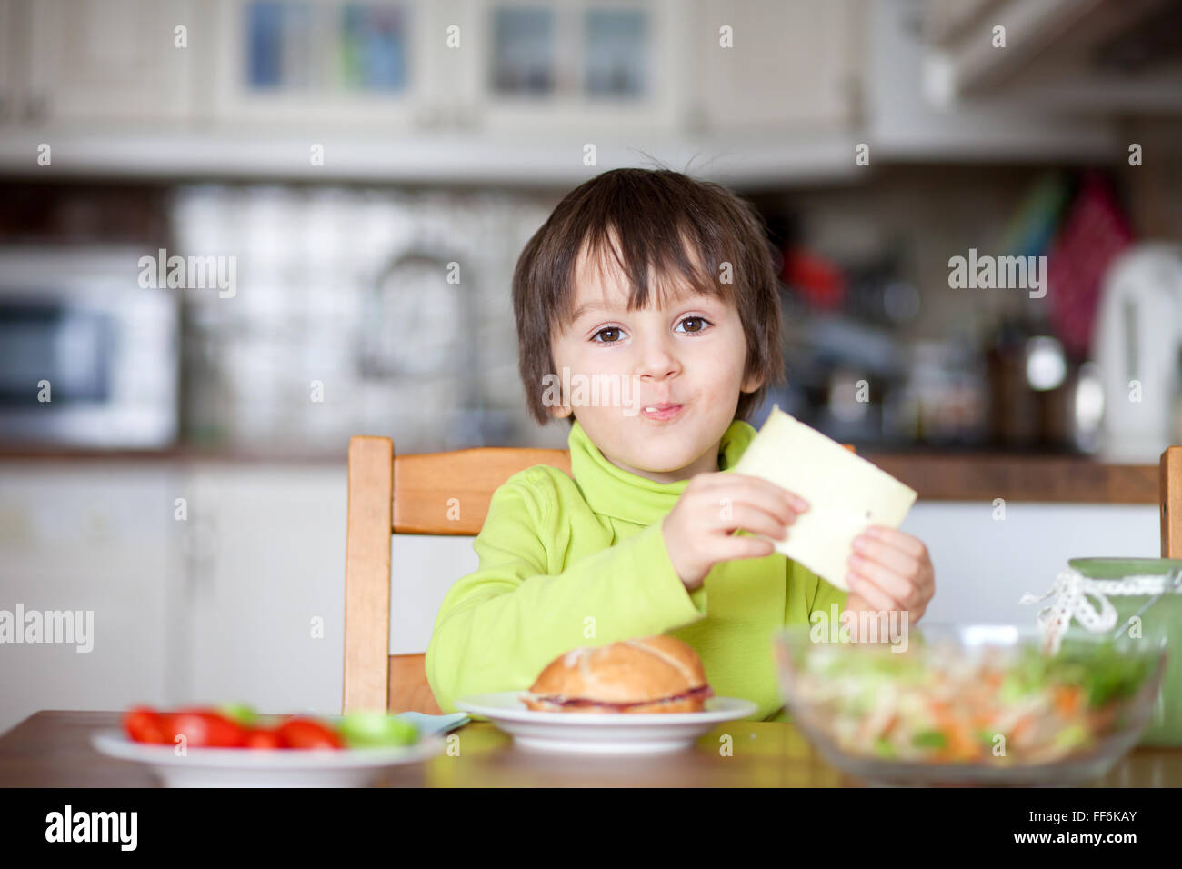 Beautiful little boy, eating sandwich at home, vegetables on the table ...