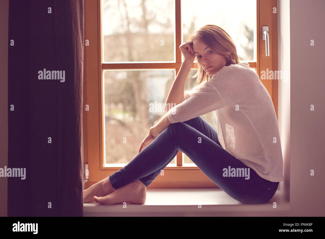 Young attractive woman, sitting on a window, looking outside, lonely ...
