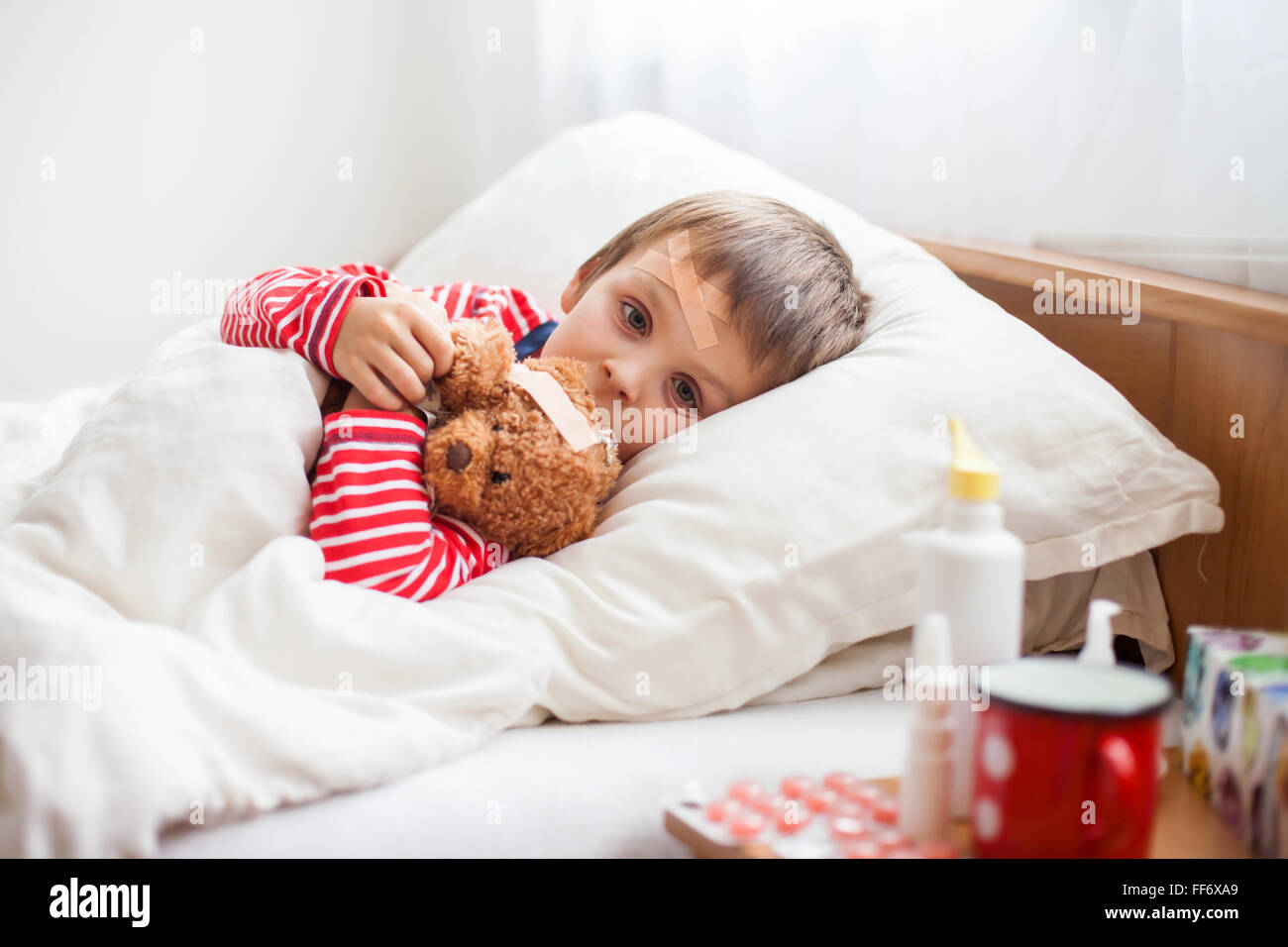 Sick child boy lying in bed with a fever, holding terry bear with band ...