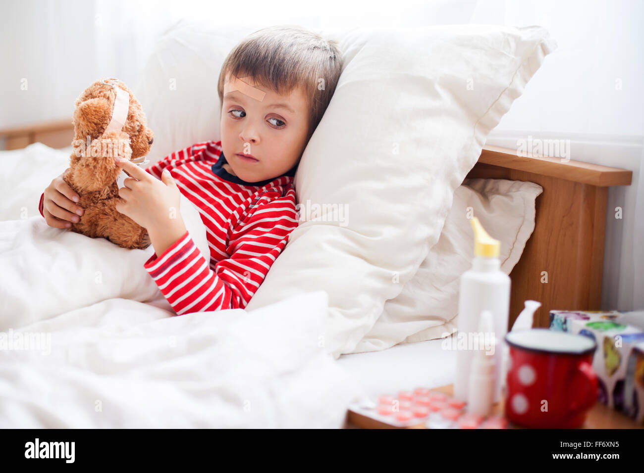 Sick child boy lying in bed with a fever, holding terry bear with band ...