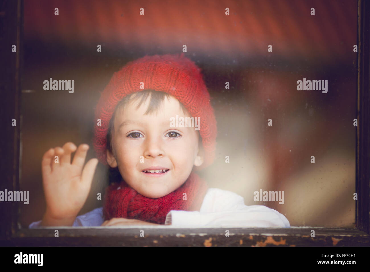 Portrait of little boy, child behind the window, wearing hat and scarf ...
