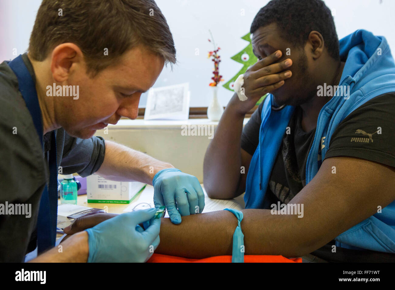 A male nurse performs a blood test whilst the patient covers his face ...
