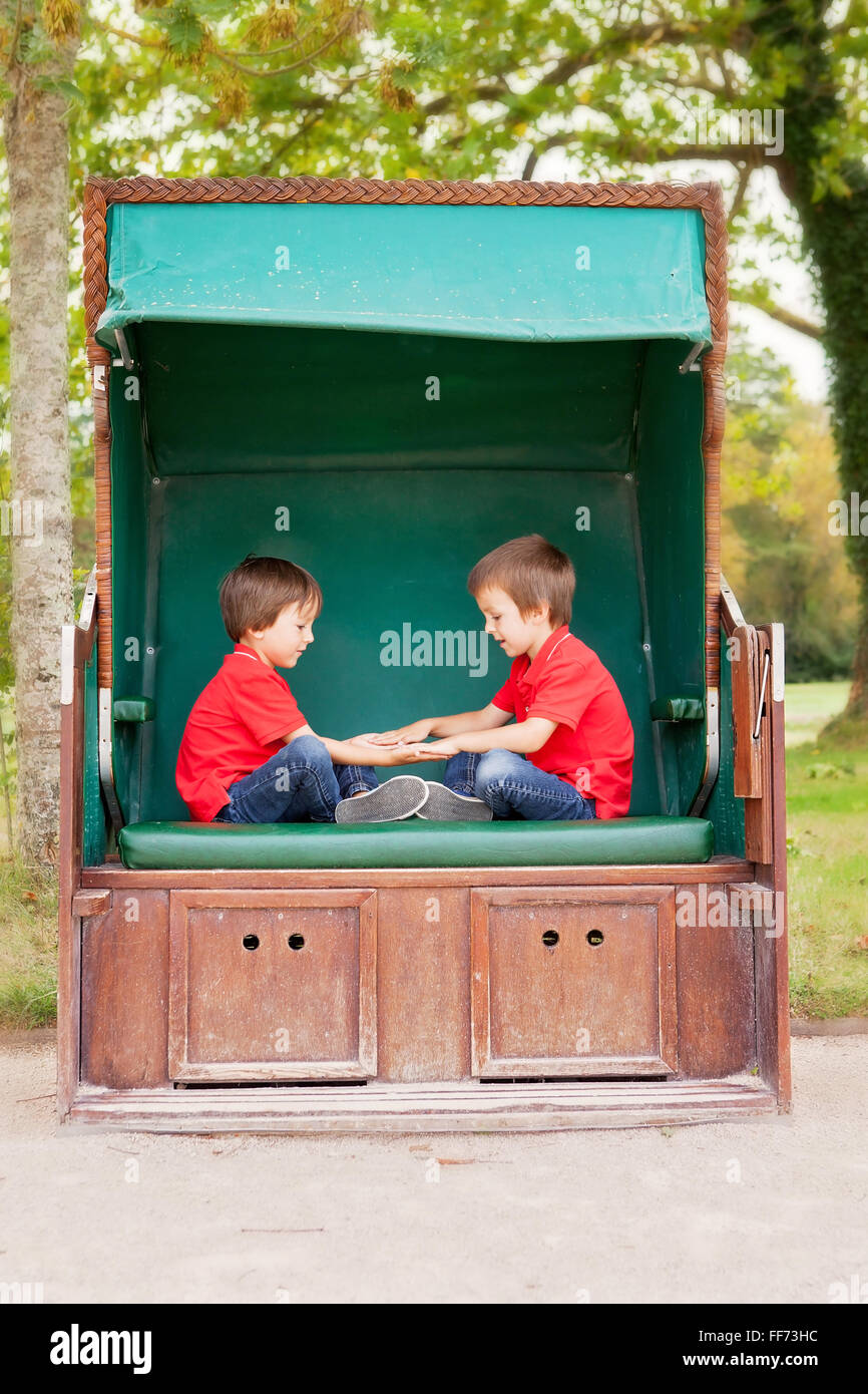 Two kids, brothers,sitting in a sheltered bench, playing hand clapping ...