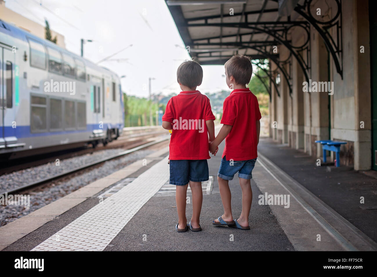Two boys, brothers, watching a train leaving a station, summertime ...