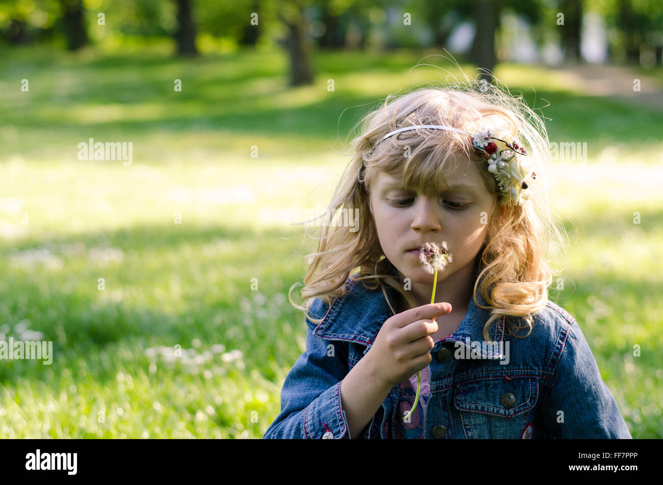 adorable blond girl sitting in green meadow and blowing dandelion ...