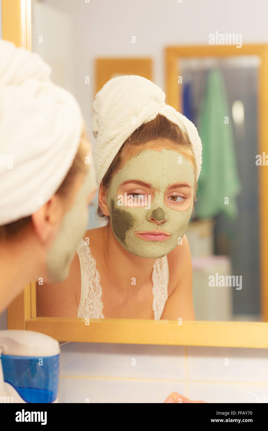 Woman removing facial dried clay mud mask with sponge in bathroom in ...