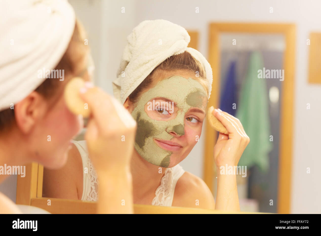 Woman removing facial dried clay mud mask with sponge in bathroom in ...
