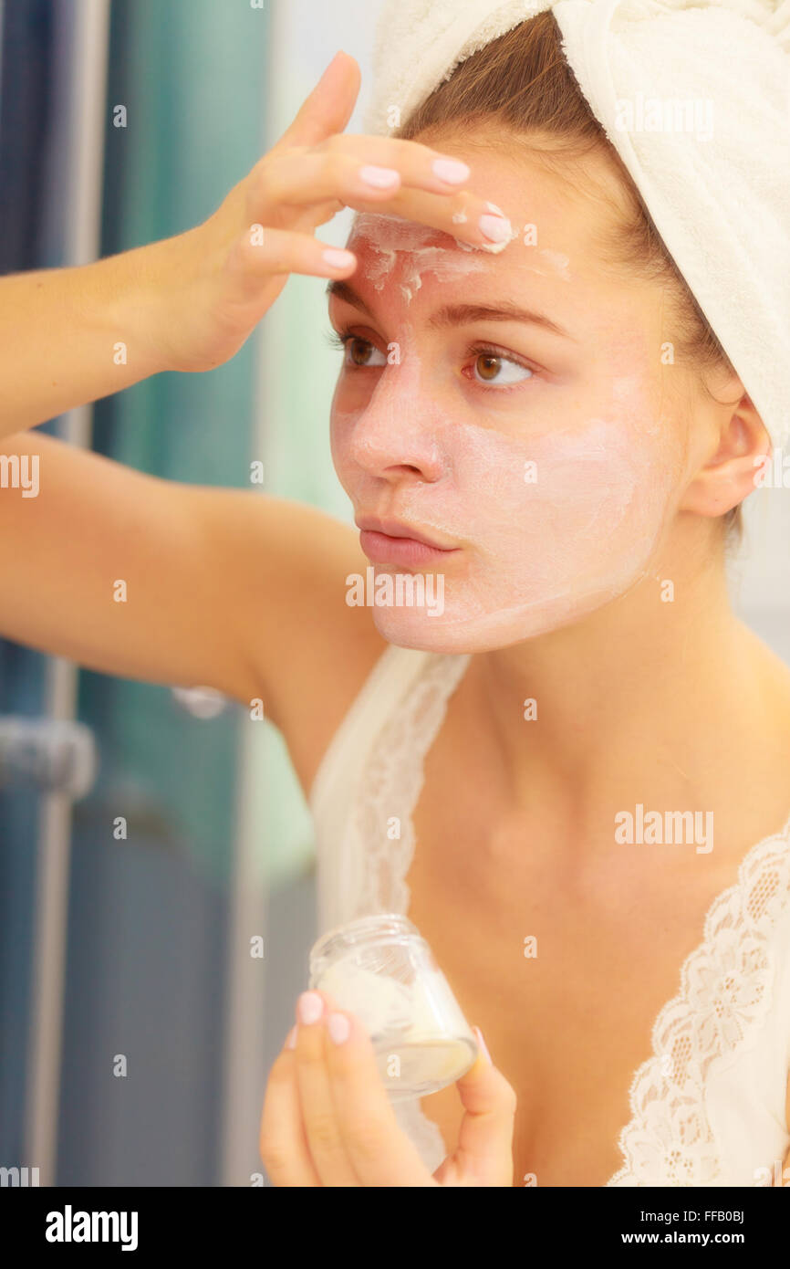 Woman applying mask moisturizing skin cream on face in bathroom. Girl ...