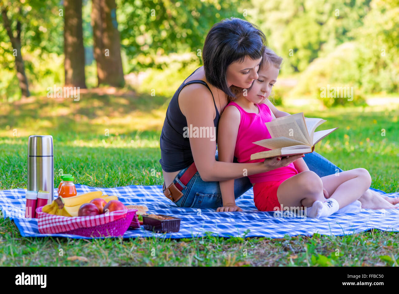 Mom and daughter reading a book on the lawn in the park Stock Photo - Alamy