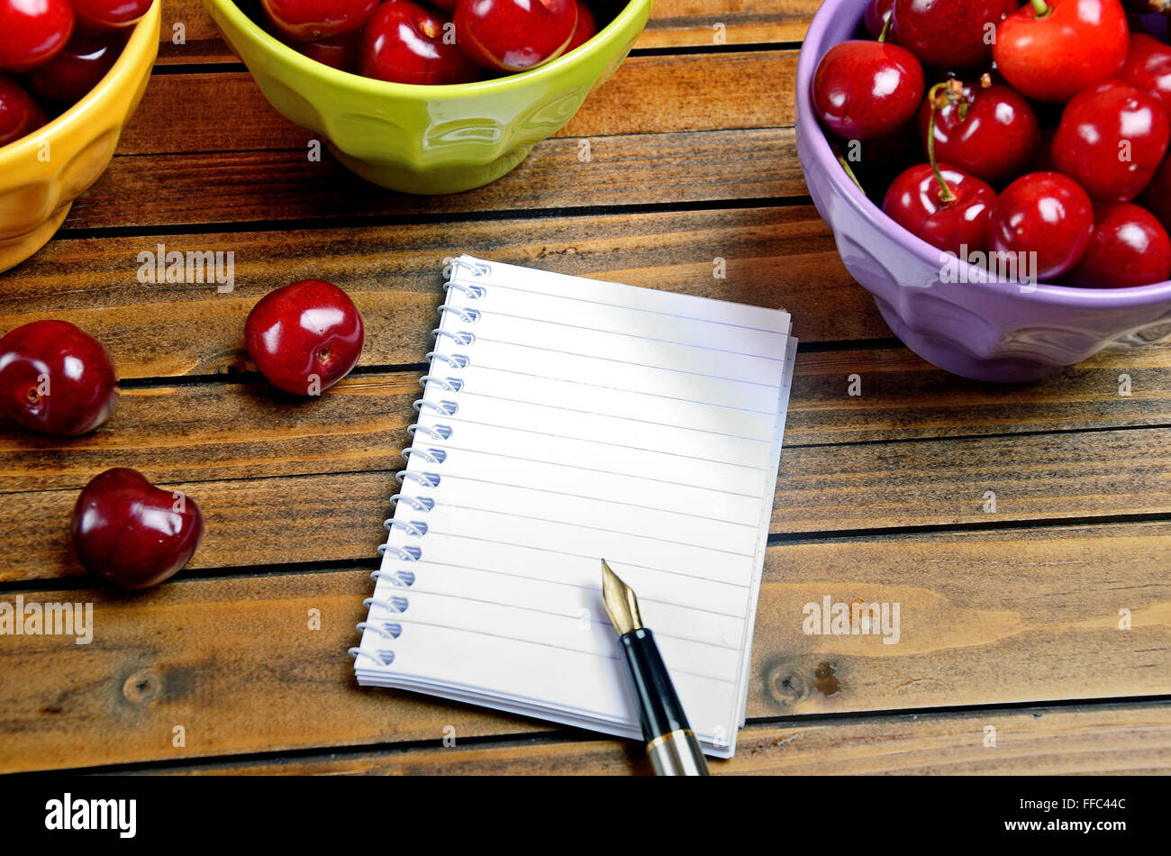 Notebook and colorful bowl with cherries on table Stock Photo - Alamy