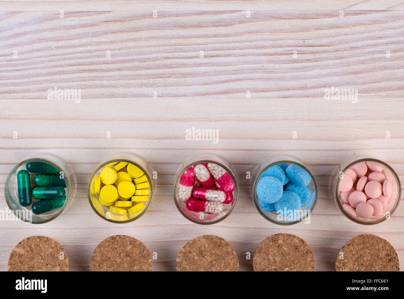 Various pills and capsules in glass containers on light wooden table ...
