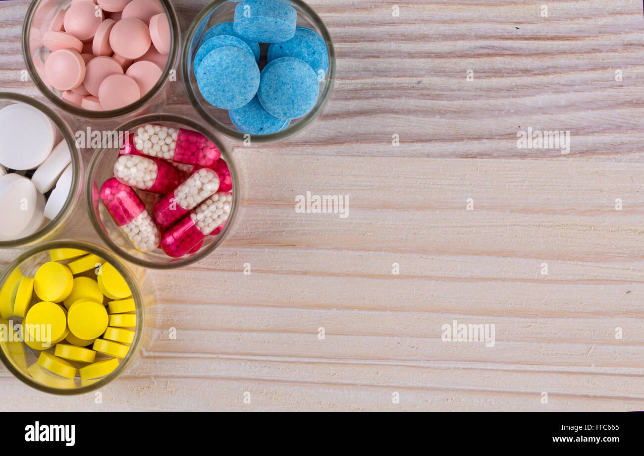 Various pills and capsules in glass containers on wooden table top view ...