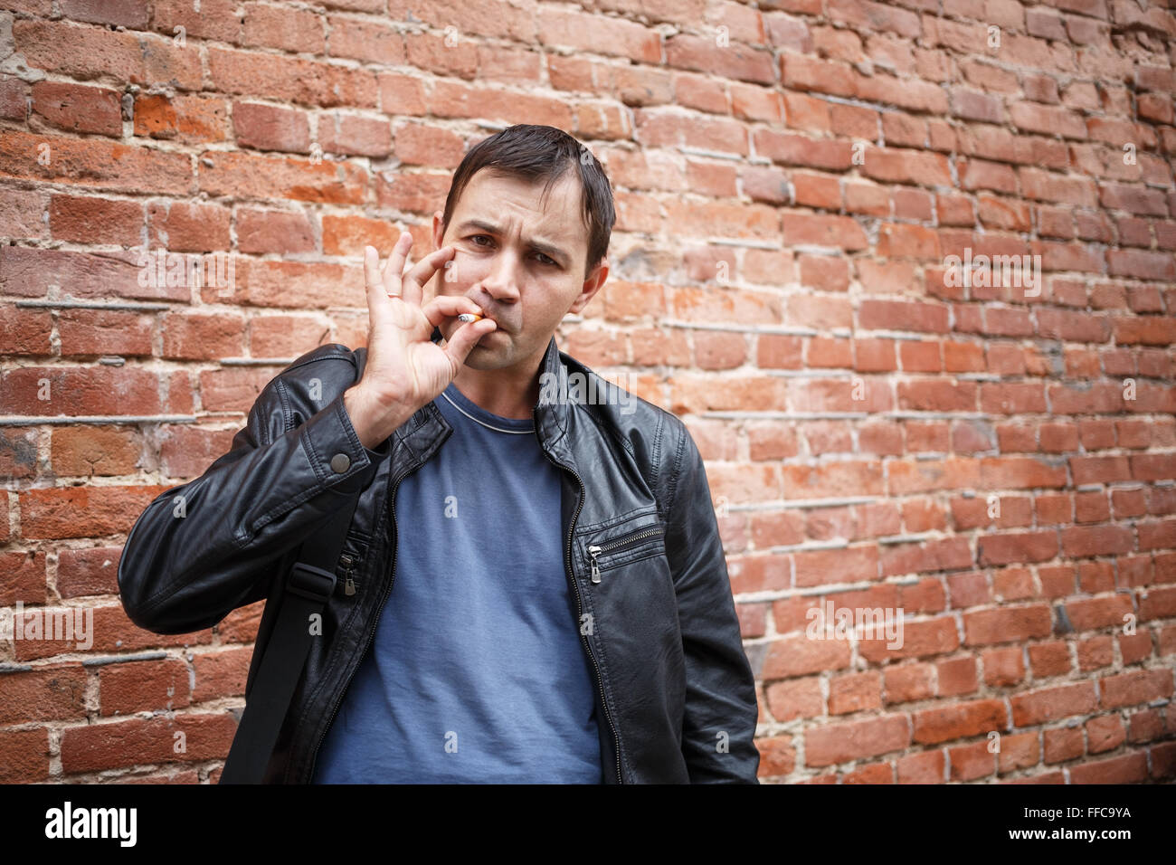 Man smoker in the background of an old brick wall. Bully in the alley ...