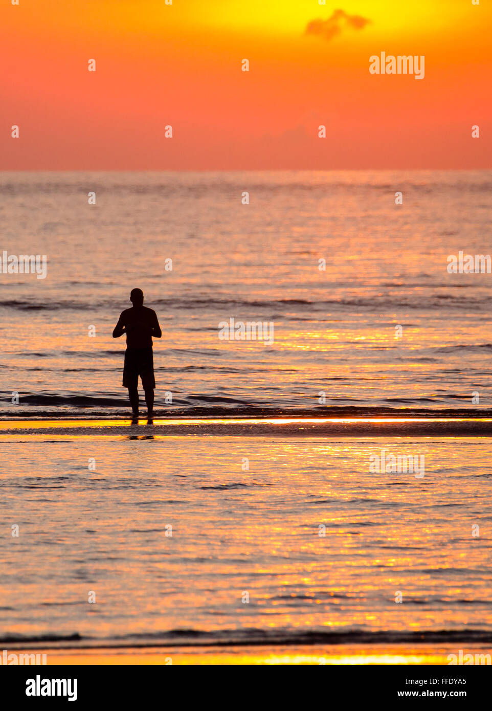 Man standing in the sea at sunset off a beach in western Sabah ...